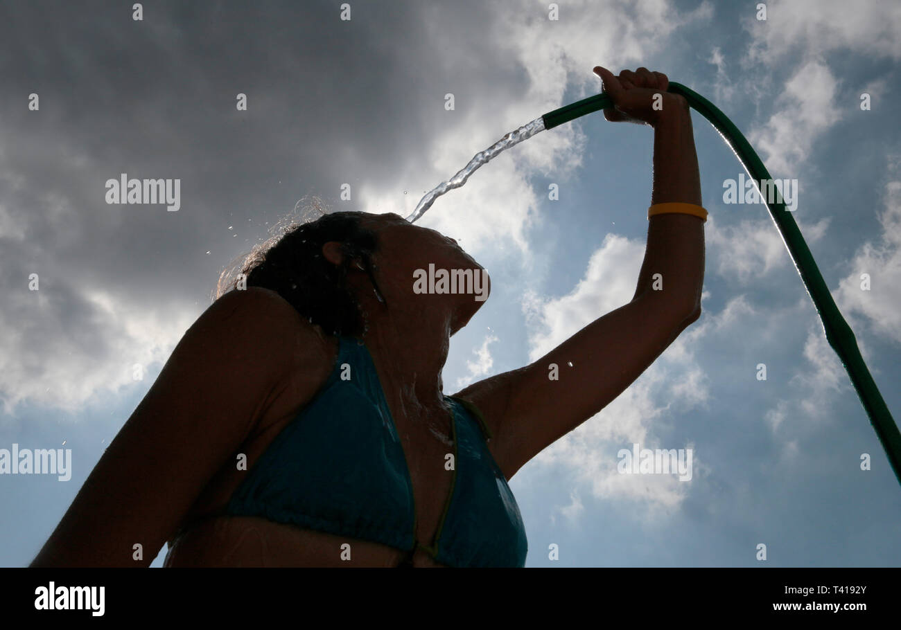 Woman in a bikini holding a hosepipe over her head in the heat Stock ...