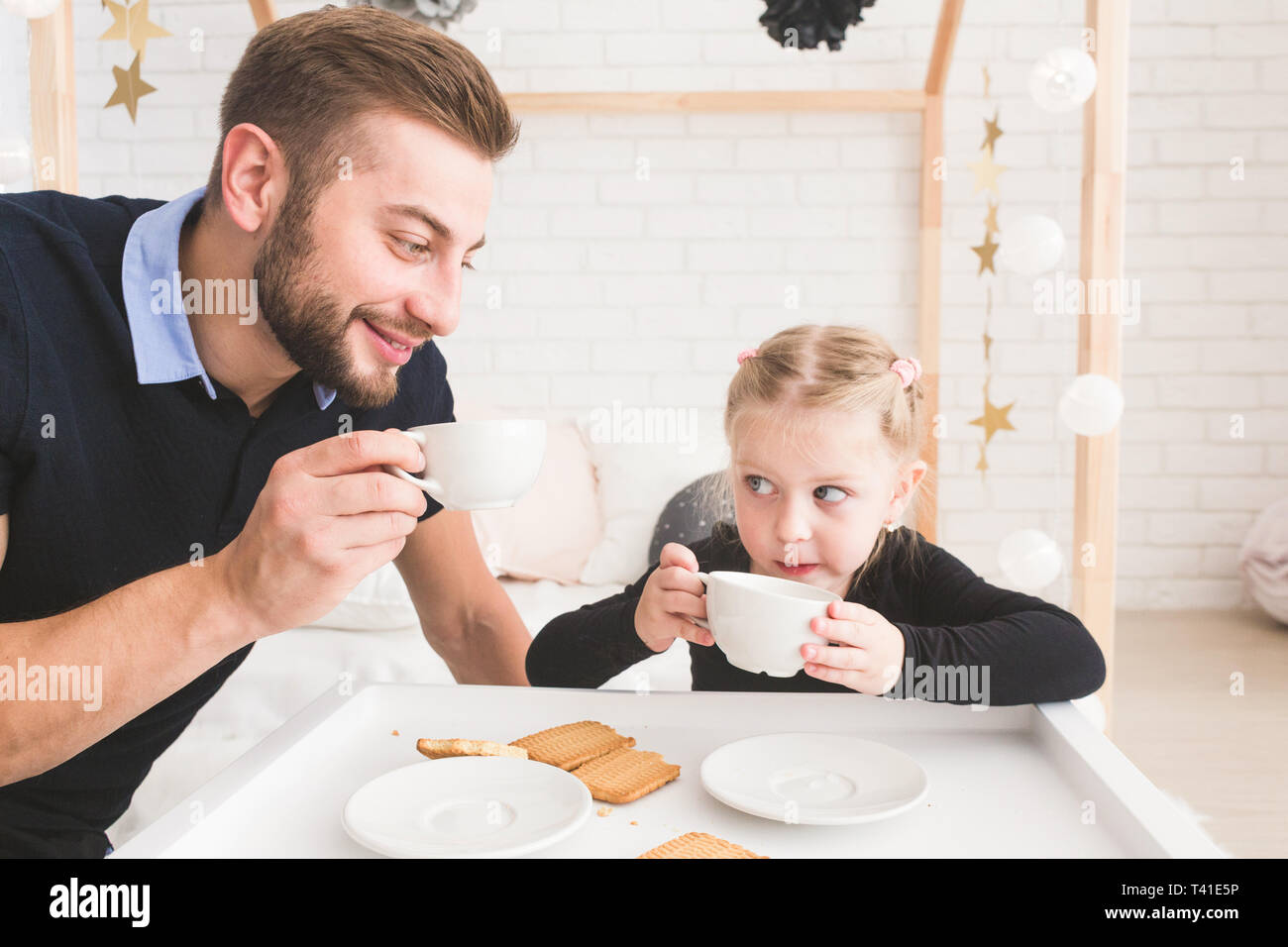 Cute little girl and her father drink tea with cookies at home Stock ...