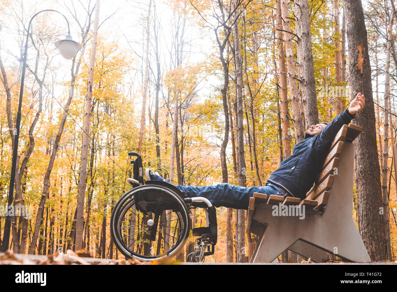 Young man resting sitting on a bench with his legs on his wheelchair ...