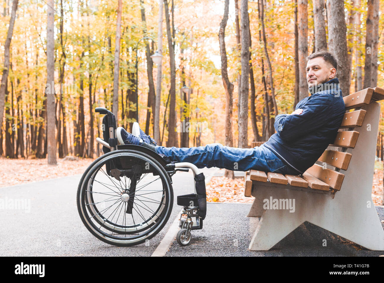 Young man resting sitting on a bench with his legs on his wheelchair ...