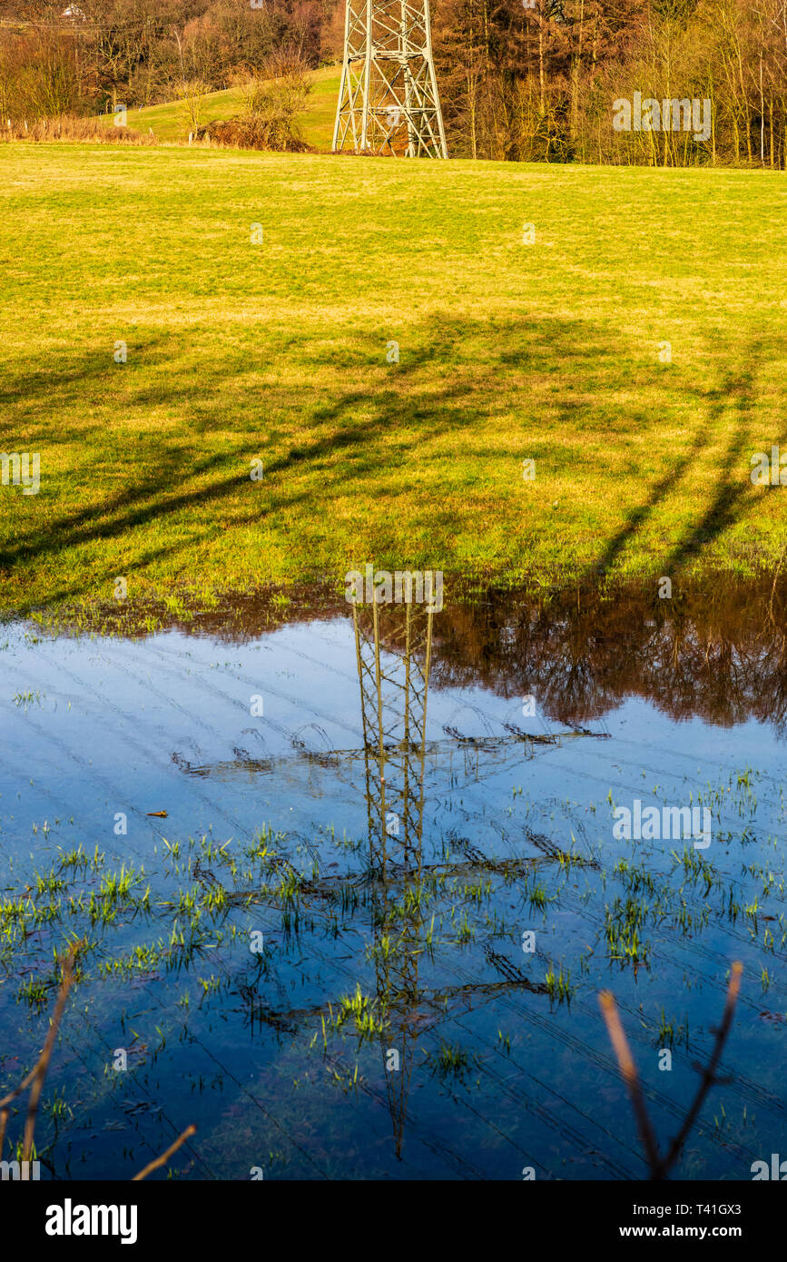 Reflection of a electricity pylon and blue sky in a puddle on a meadow ...