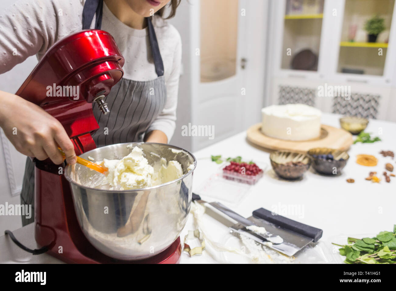 Young female confectioner whips cream in a metal bowl in a red electric ...
