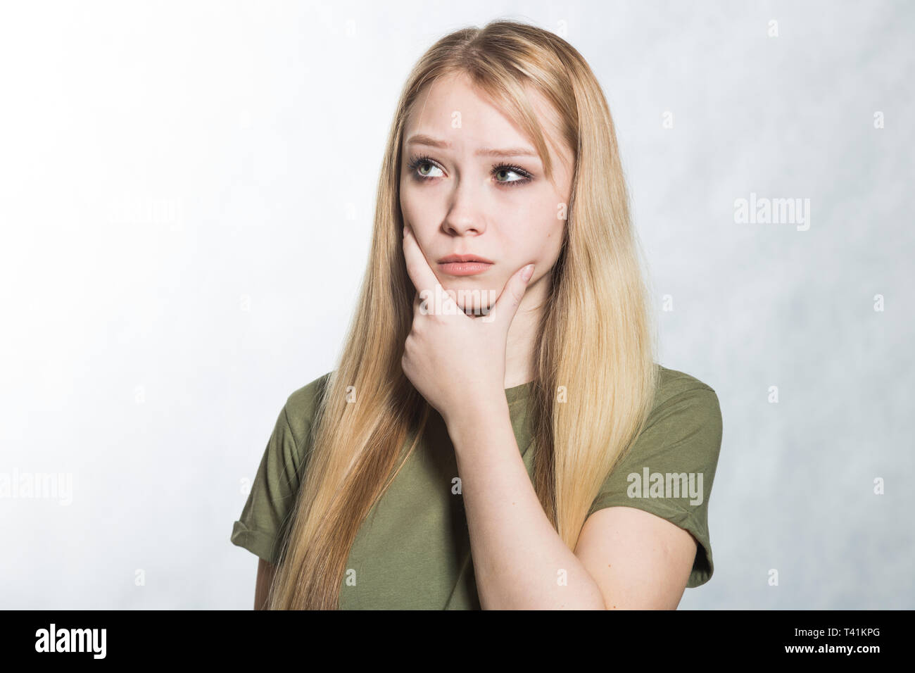 Embarrassed unsure young woman holds her chin and purses his lips ...