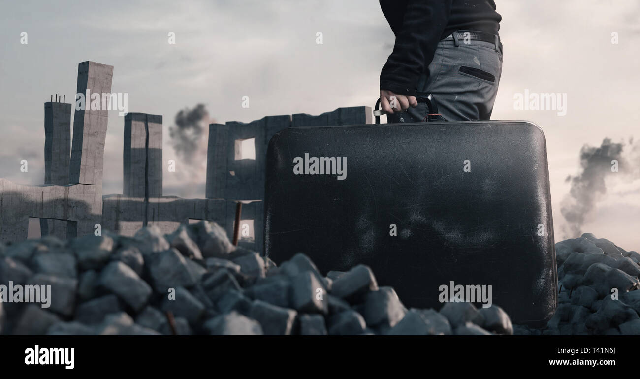 homeless man with suitcase in the hand in front of damaged house walls ...