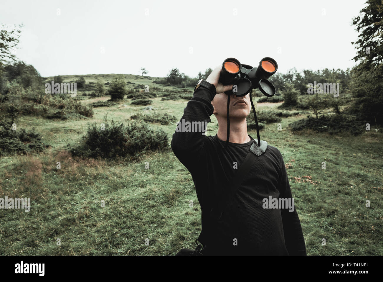 Hiker looking through binoculars in front of hills and mountain range ...