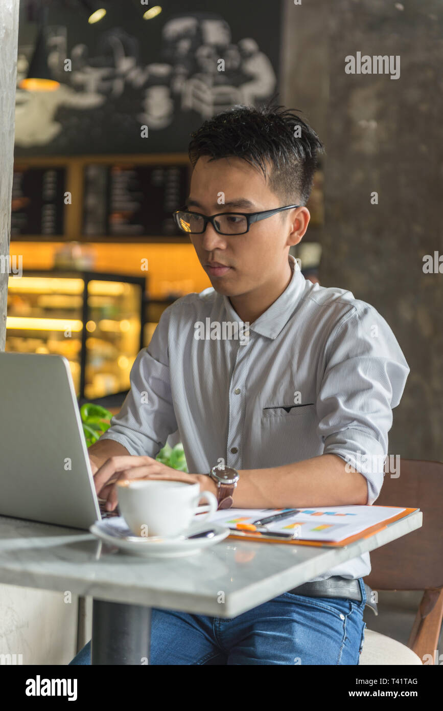 Vertical photo of Asian freelancer working on laptop Stock Photo - Alamy