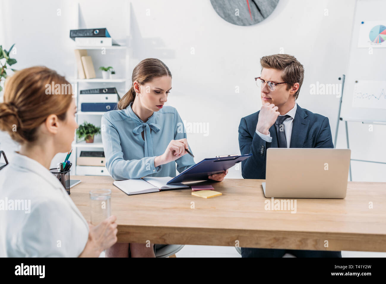 attractive recruiter talking and looking at clipboard near coworker in ...