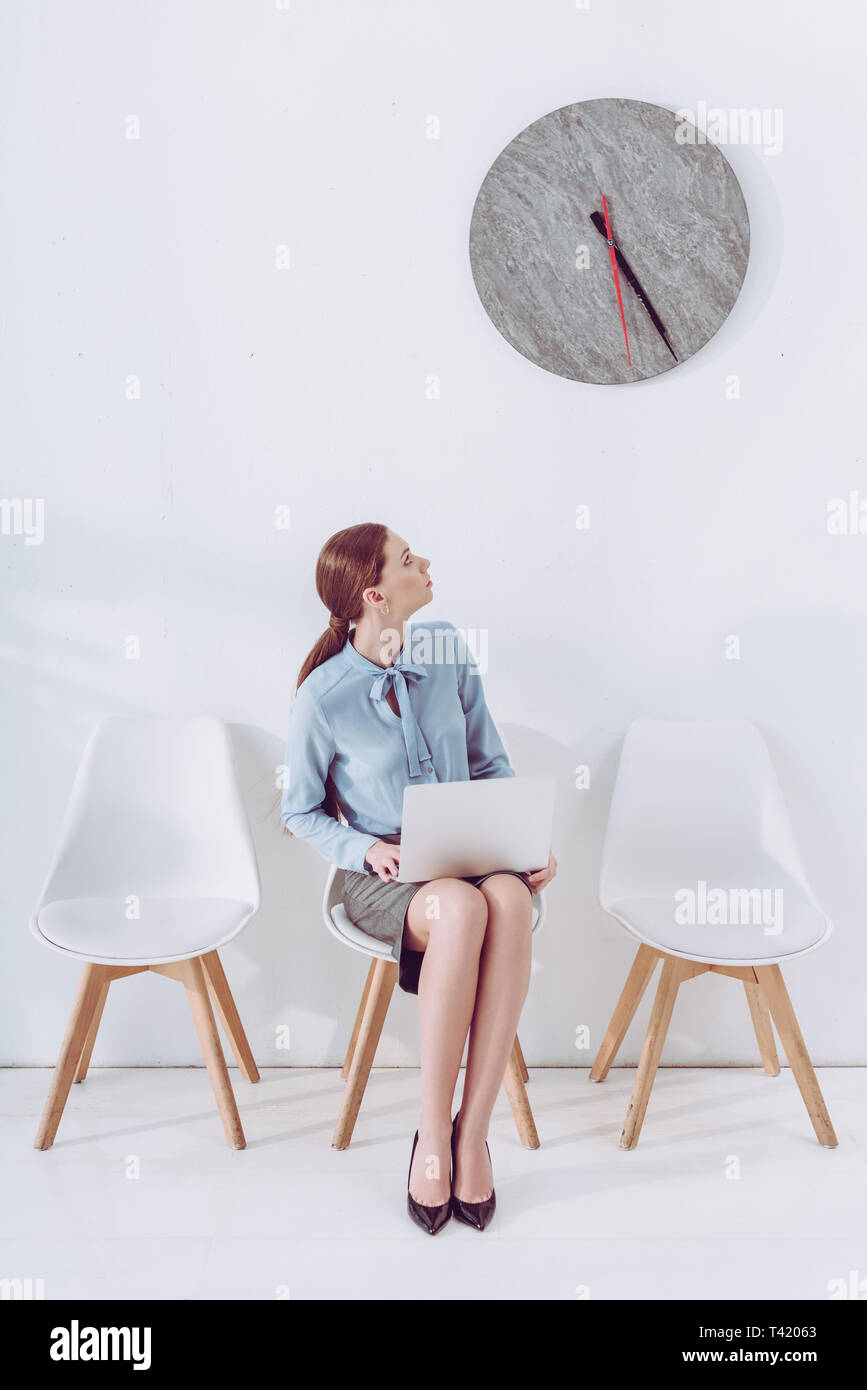 employee sitting on chair with laptop and looking at clock Stock Photo ...