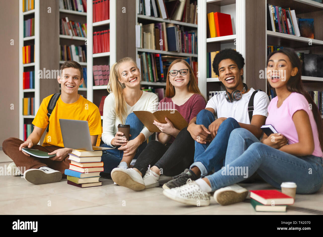 Group of diverse teenage classmates sitting on library floor Stock ...