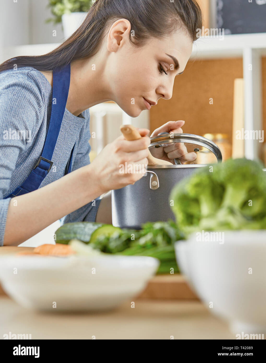 Beautiful girl is tasting food and smiling while cooking in kitchen at ...
