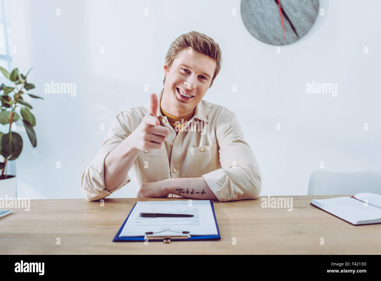 happy recruiter pointing with finger while sitting near clipboard and ...