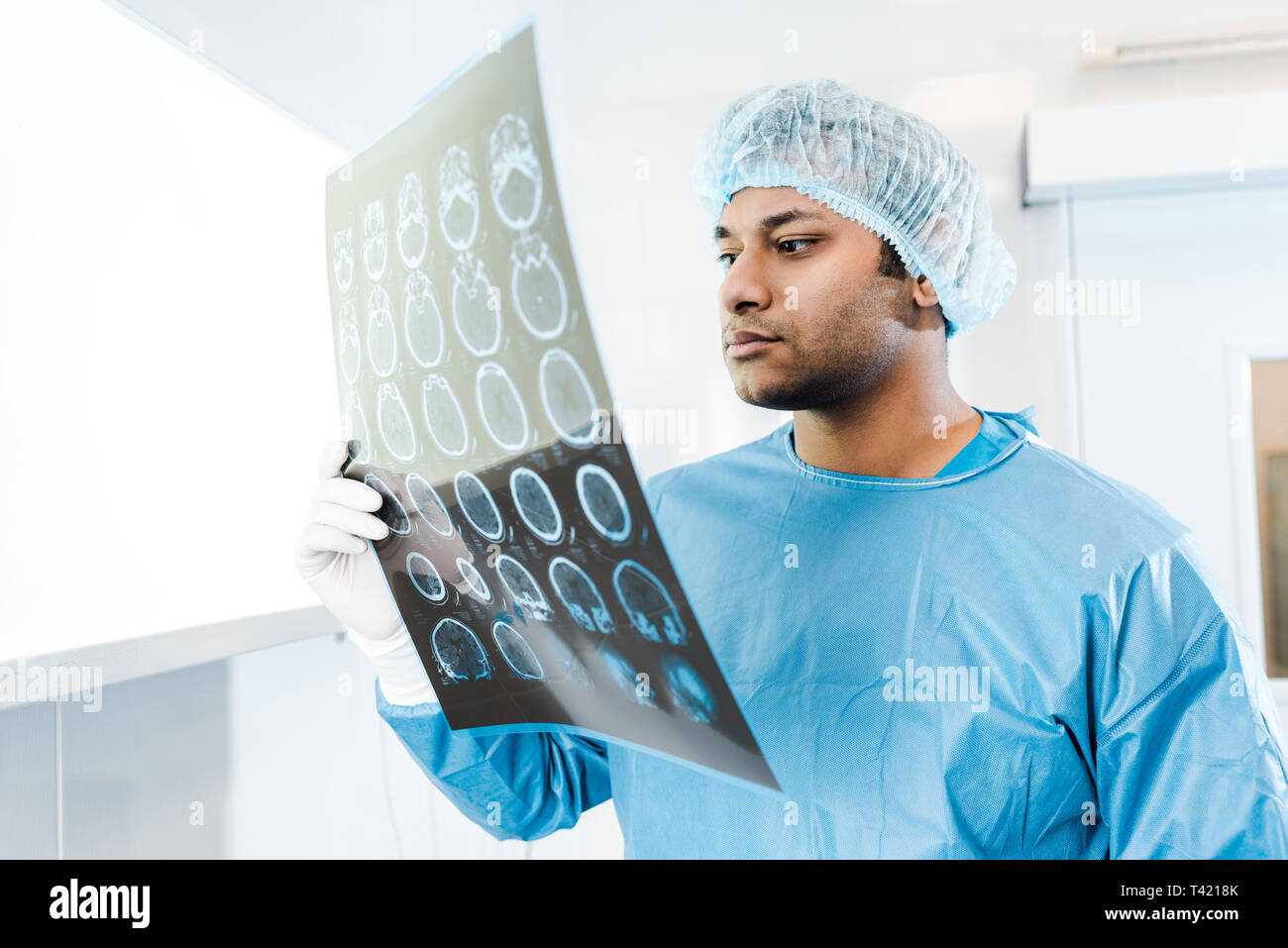 handsome doctor in medical cap and uniform holding and looking at x-ray ...