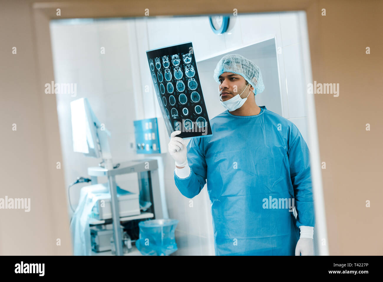 handsome doctor in uniform and medical cap looking at x-ray in clinic ...
