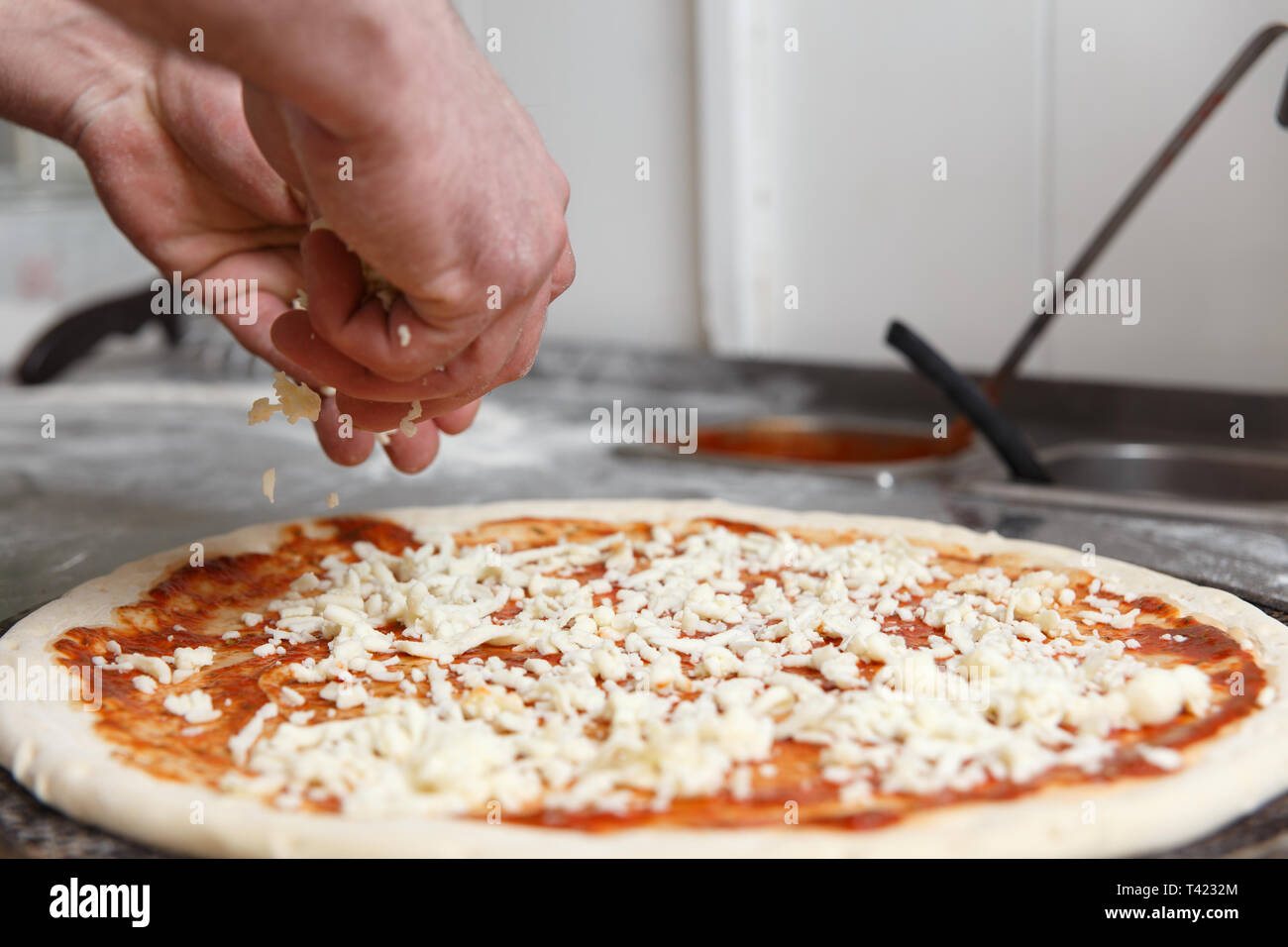 The hands of chef sprinkles the pizza with cheese in restaurant kitchen ...