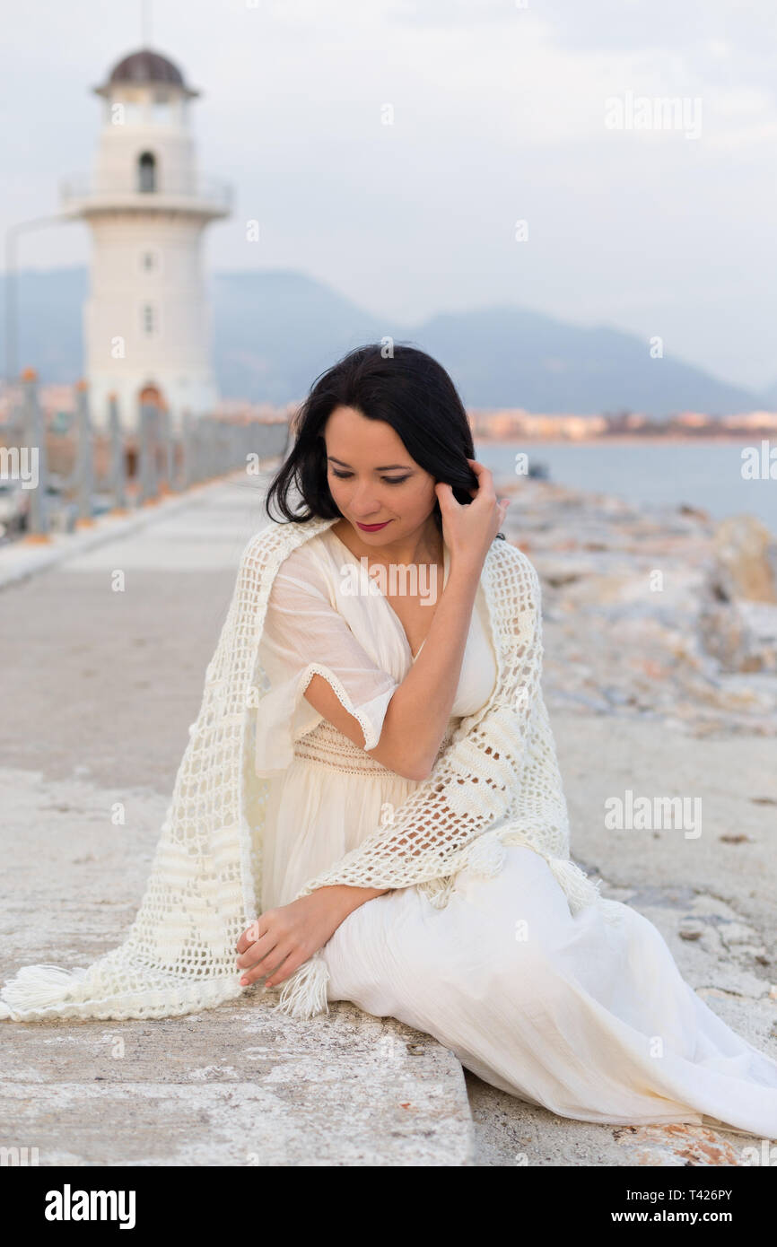 Brunette female dressed in boho style clothes sitting on the rocks with ...