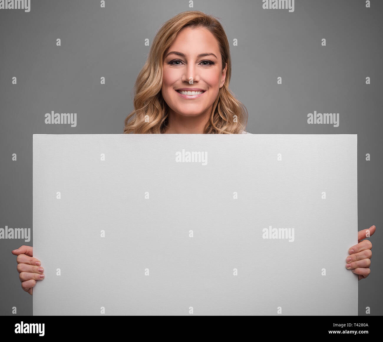 Attractive blonde holds white blank empty poster for your text or image ...