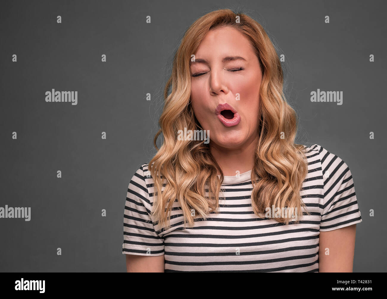 A young woman is squinting a sour grimace while standing against grey ...