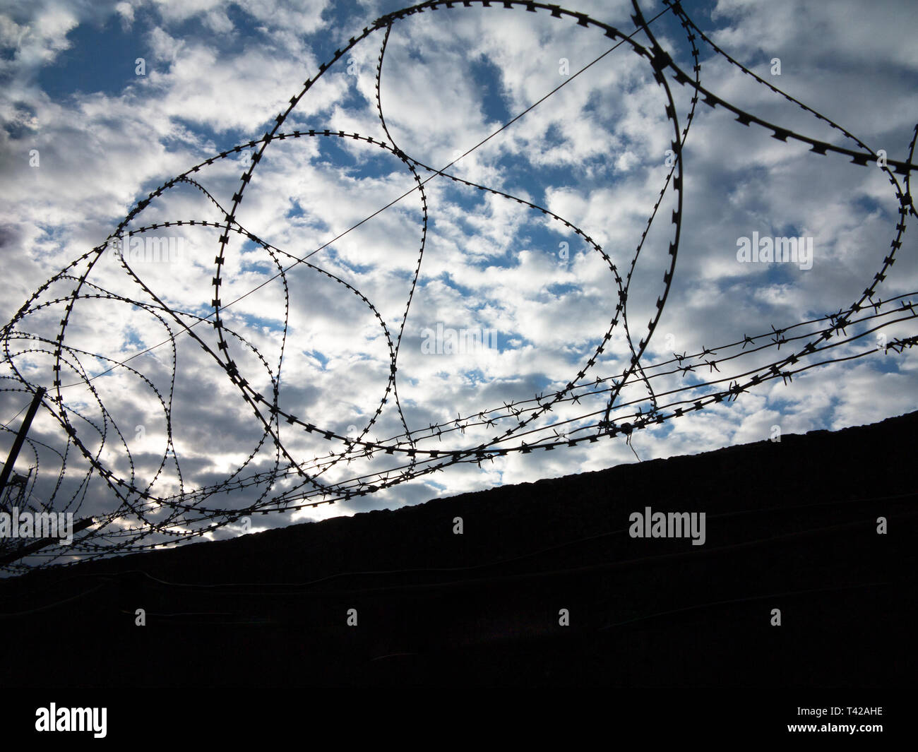 Thorned wire above concrete fence with fancy clouds on the background ...