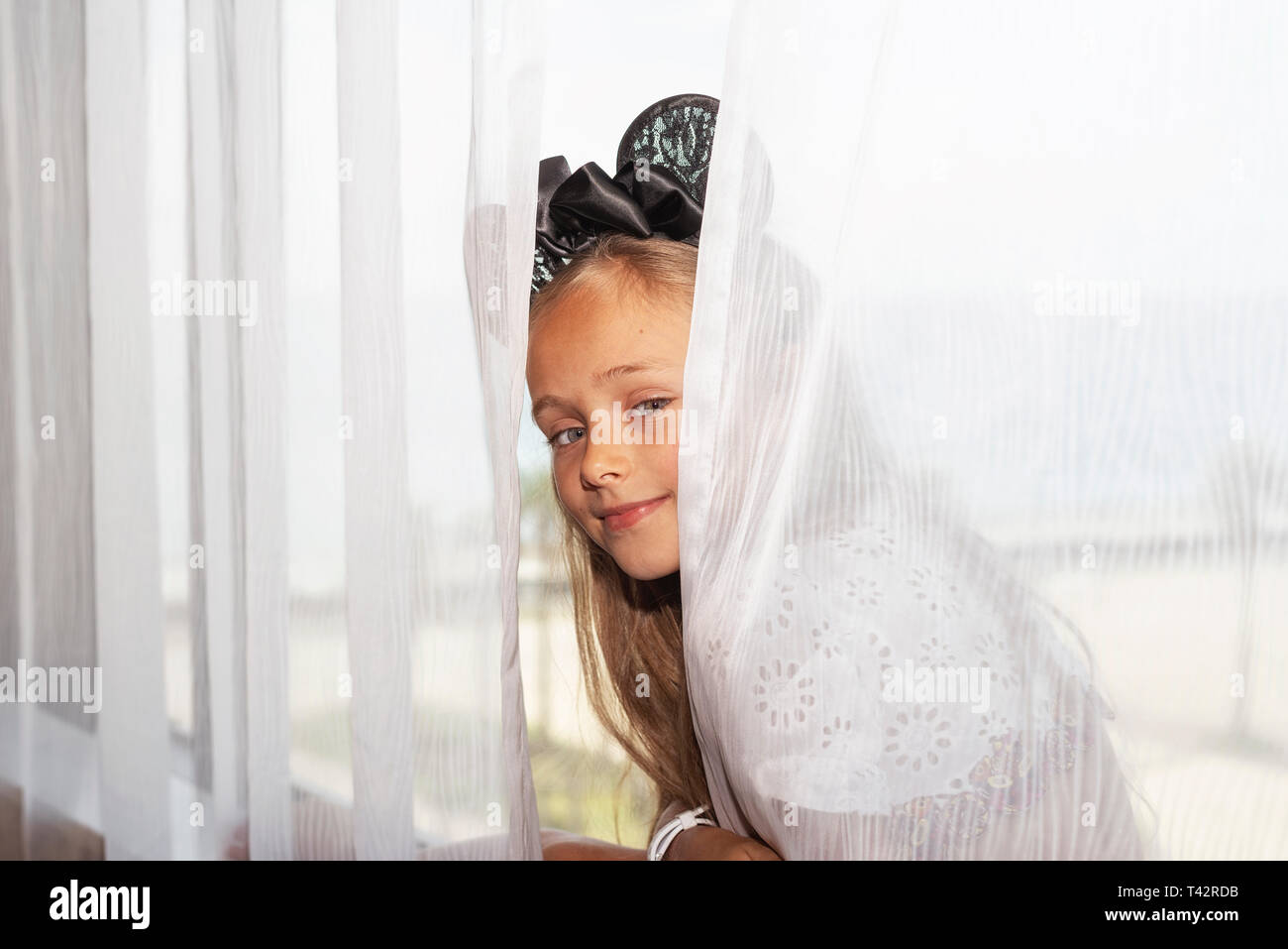 The little girl is sitting on the window and looking out from behind ...