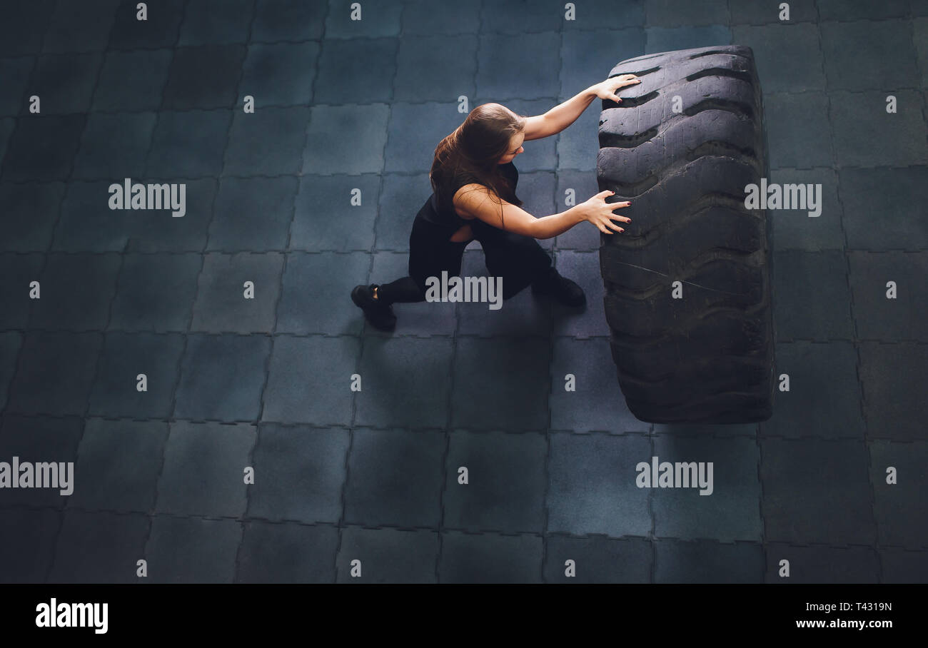 Fit female athlete working out with a huge tire, turning and carry in ...