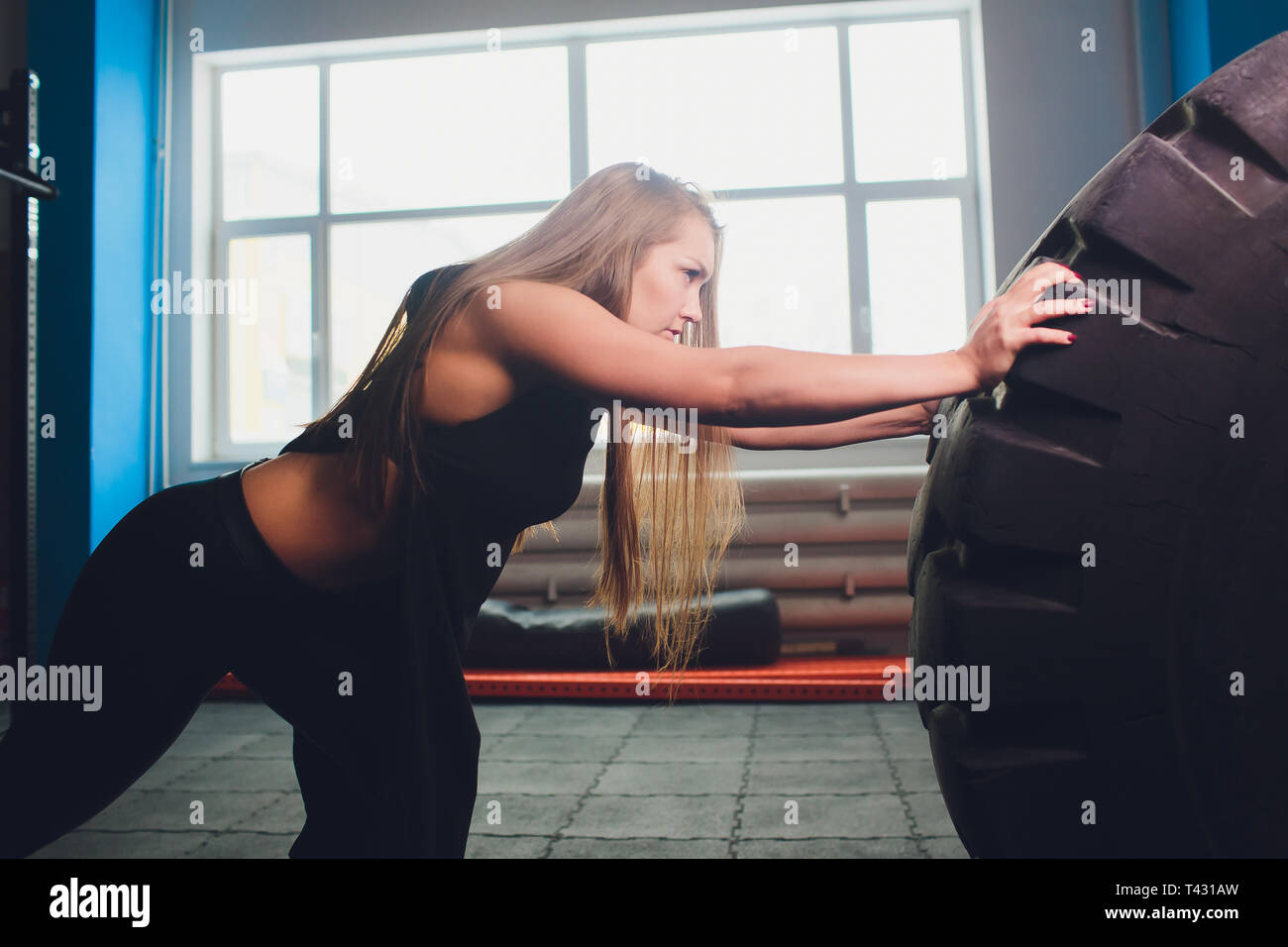 Fit female athlete working out with a huge tire, turning and carry in ...