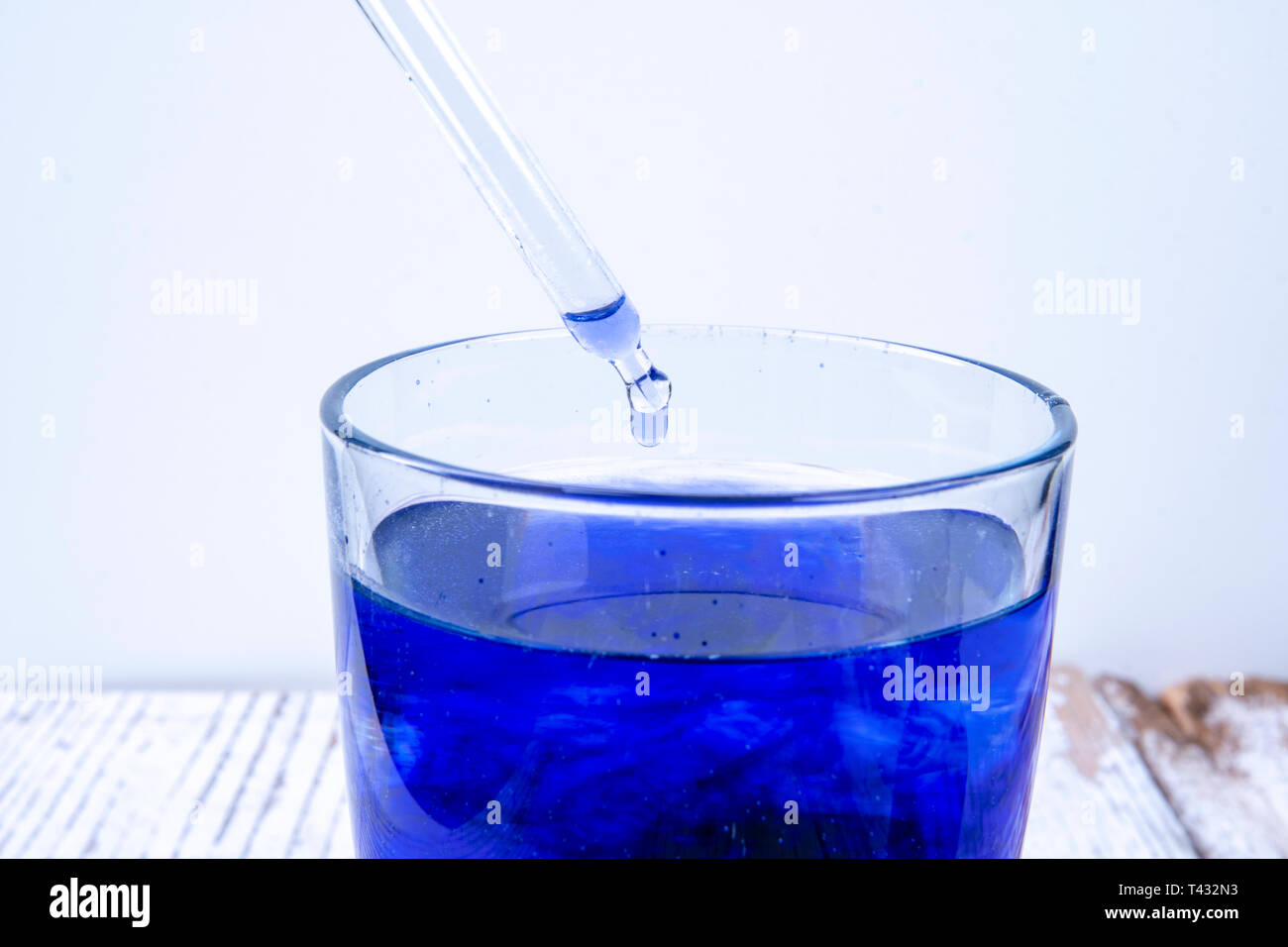 Pipette drips into a glass with blue liquid Stock Photo - Alamy
