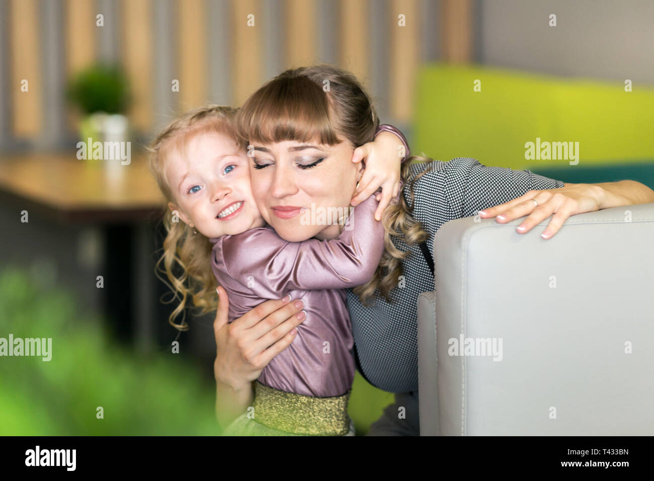 A girl of 4-5 years old is hugging the neck of her young mother with ...