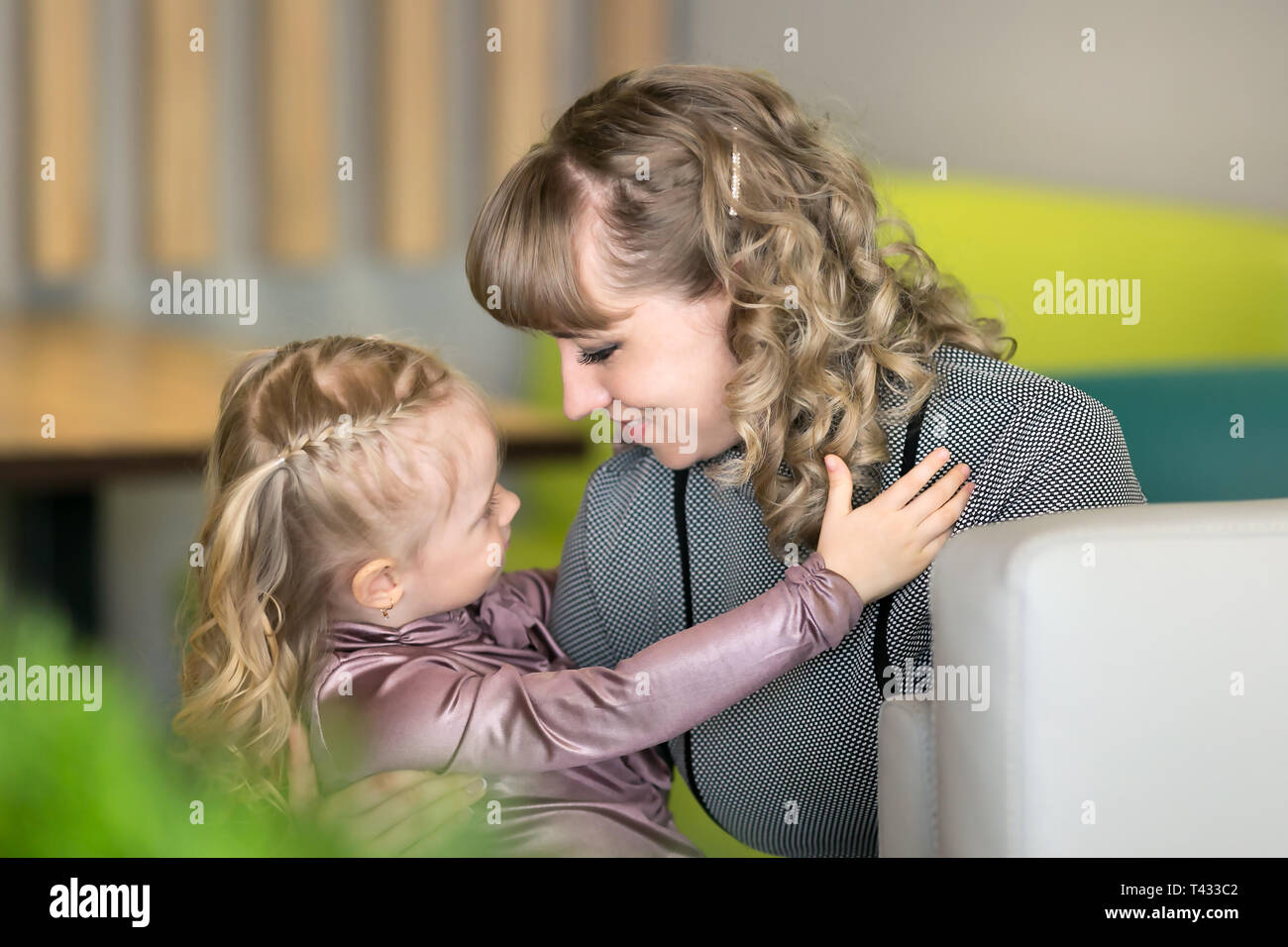 A girl of 4-5 years old is hugging the neck of her young mother with ...