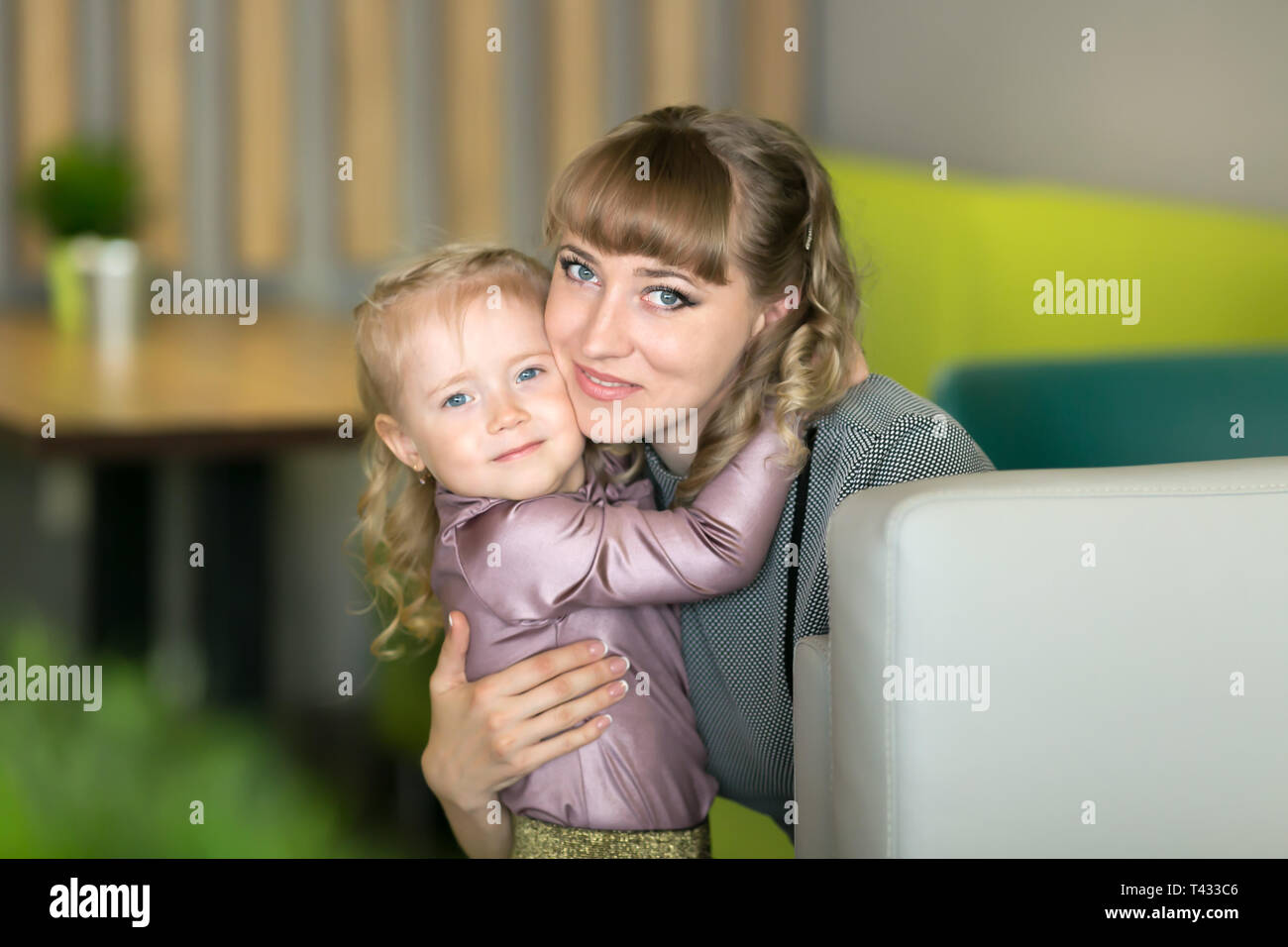 A girl of 4-5 years old is hugging the neck of her young mother with ...