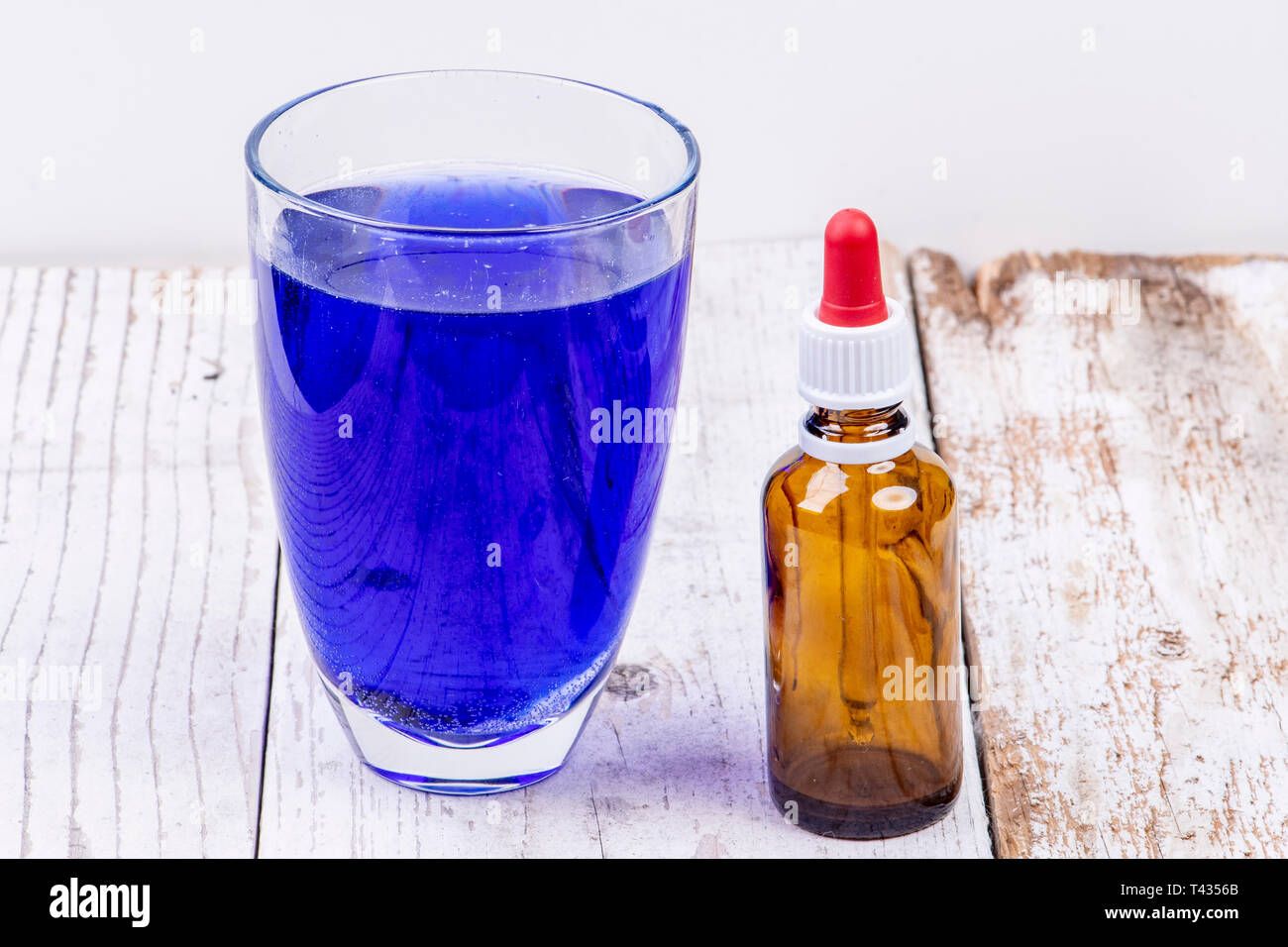 a glass with blue liquid next to a brown medicine bottle with pipette ...