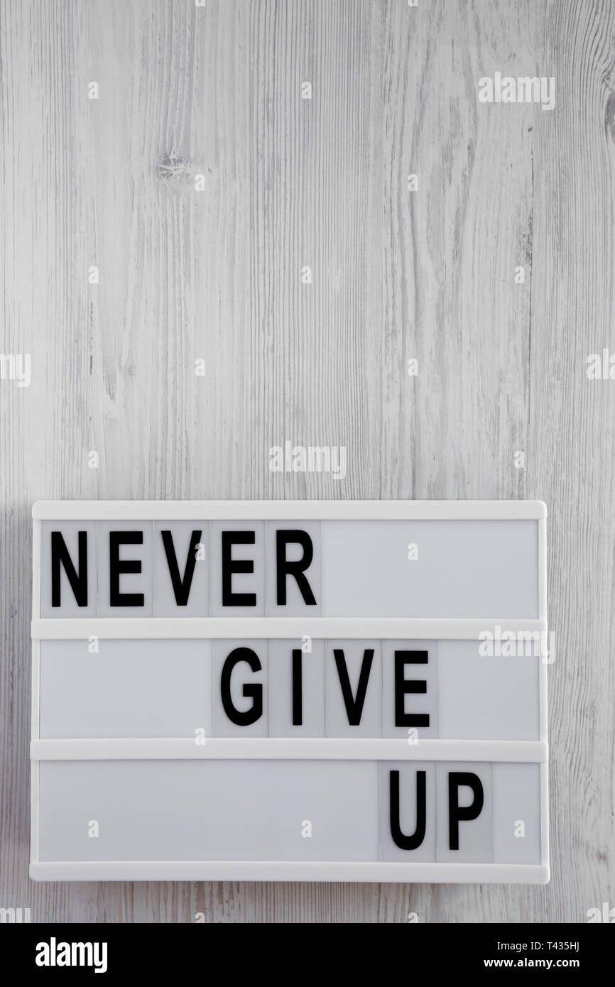 'Never give up' words on modern board over white wooden surface. Flat ...