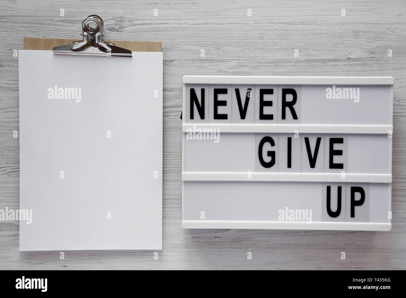 'Never give up' words on lightbox, clipboard with blank sheet of paper ...