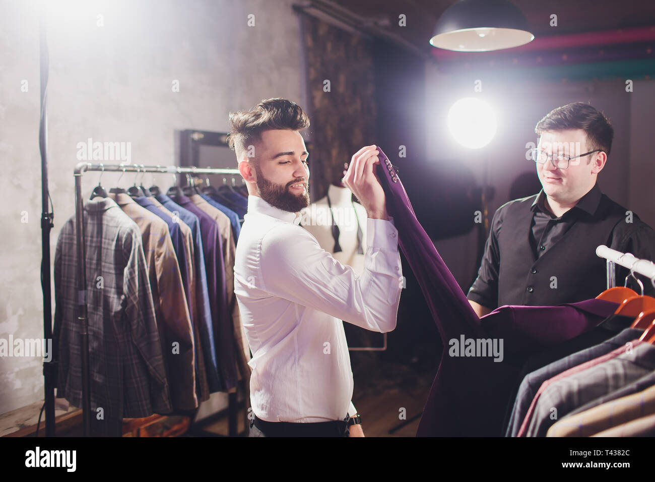 Male customer at shopping mall trying business clothes, shop assistant ...