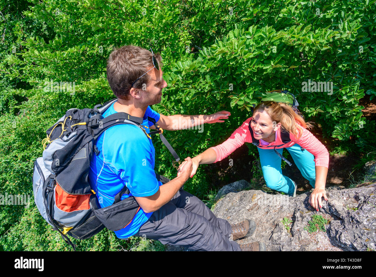 Man helping woman to climb up in rocky nature Stock Photo - Alamy