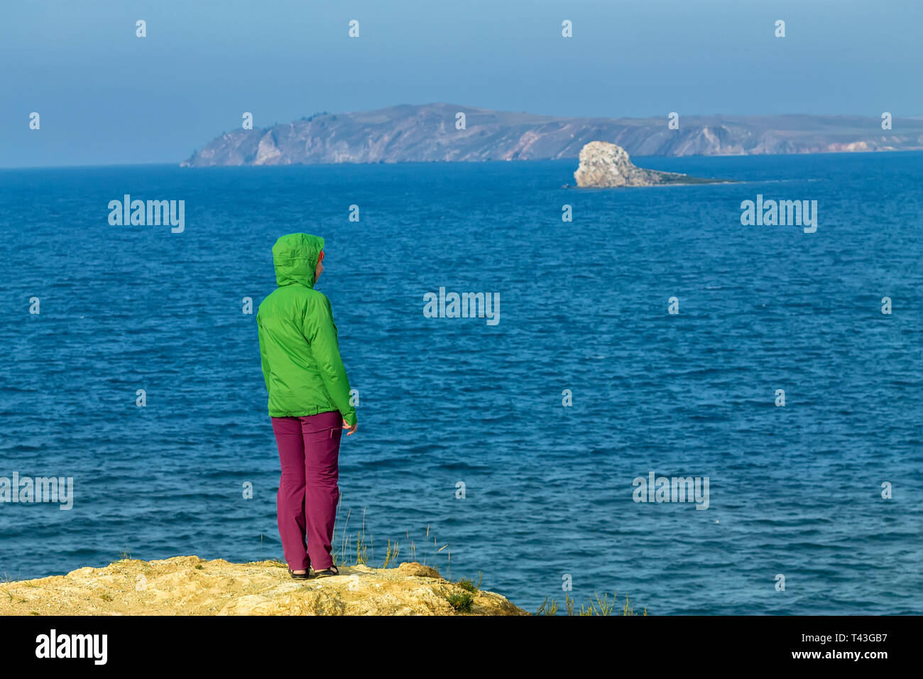tourist girl walks in yellow grass across a field overlooking the water ...