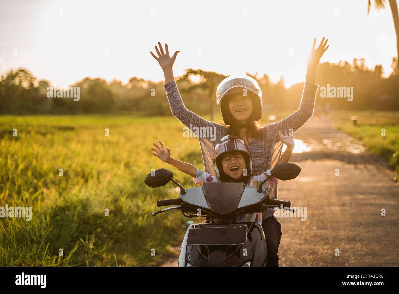portrait of happy mother raise her arm while riding motorcycle with her ...