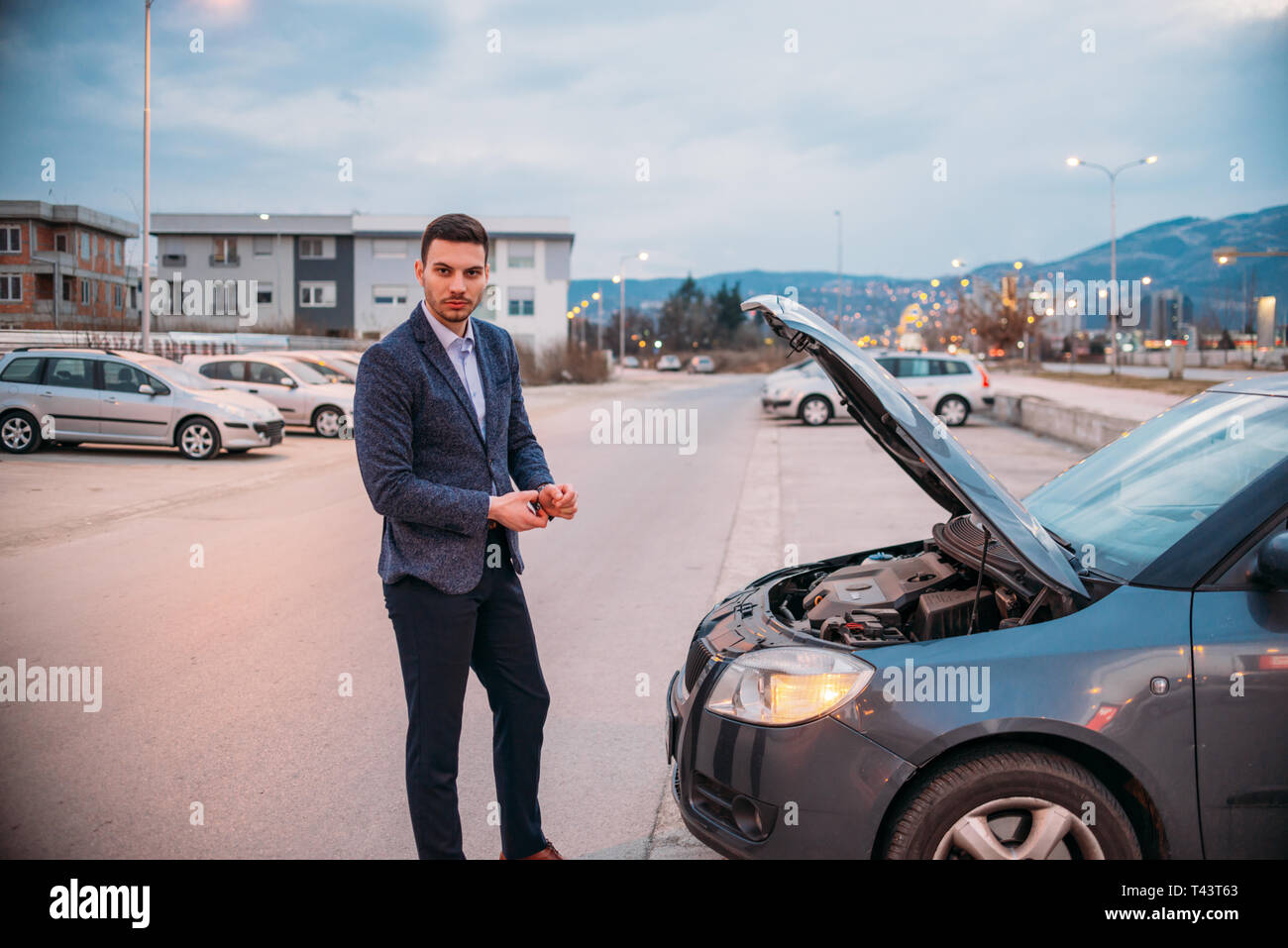 A tired worker is standing next to his car formally dressed and looking ...