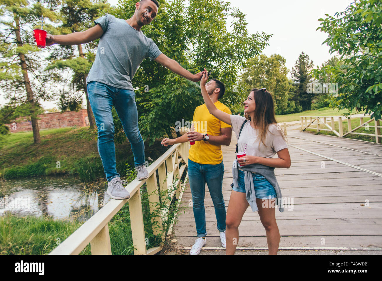 Two people holding their friends who is standing on the bridge fence ...