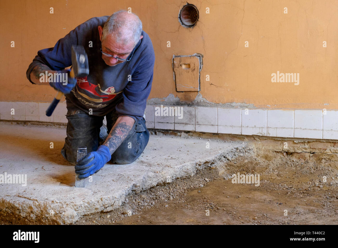 man using hammer and chisel to dig up concrete floor during house ...