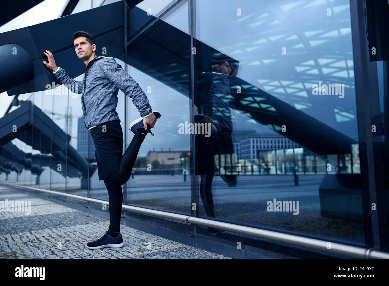 Active man doing his stretching workout next to modern building with ...
