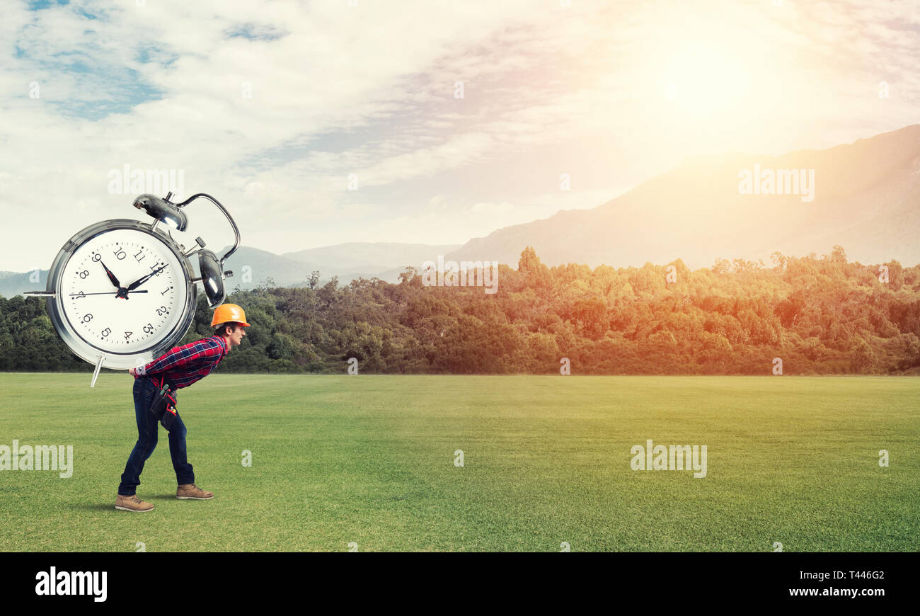 Builder man in helmet carrying alarm clock on back Stock Photo - Alamy