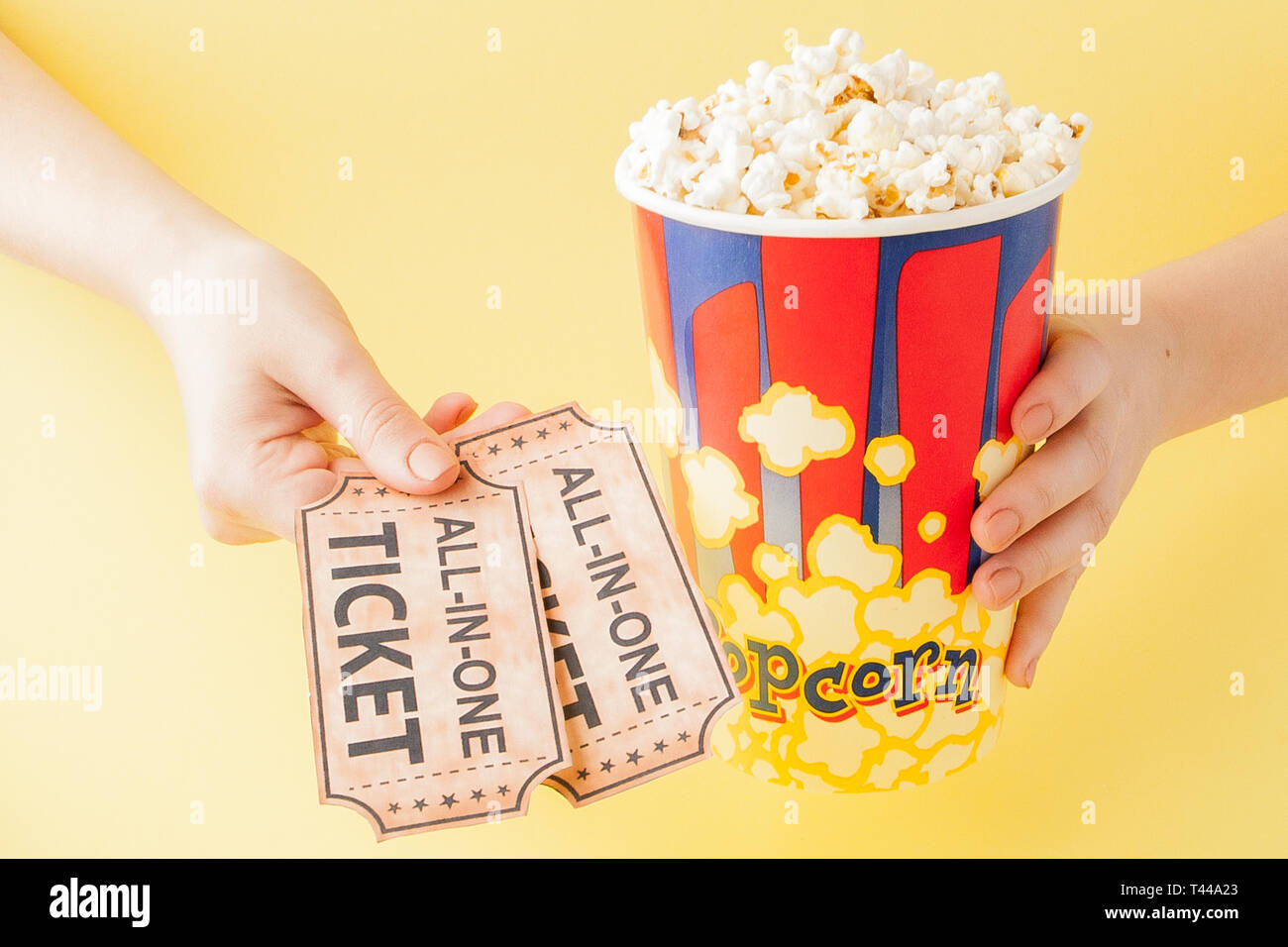 Hand takes a movie tickets and popcorn from a paper cup on a yellow ...