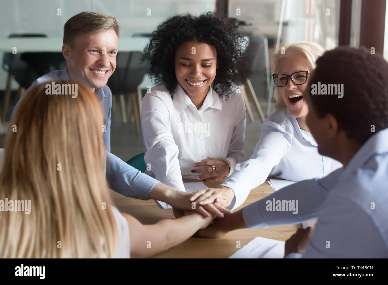 Happy multi ethnic employees stacking hands engaged in team building ...