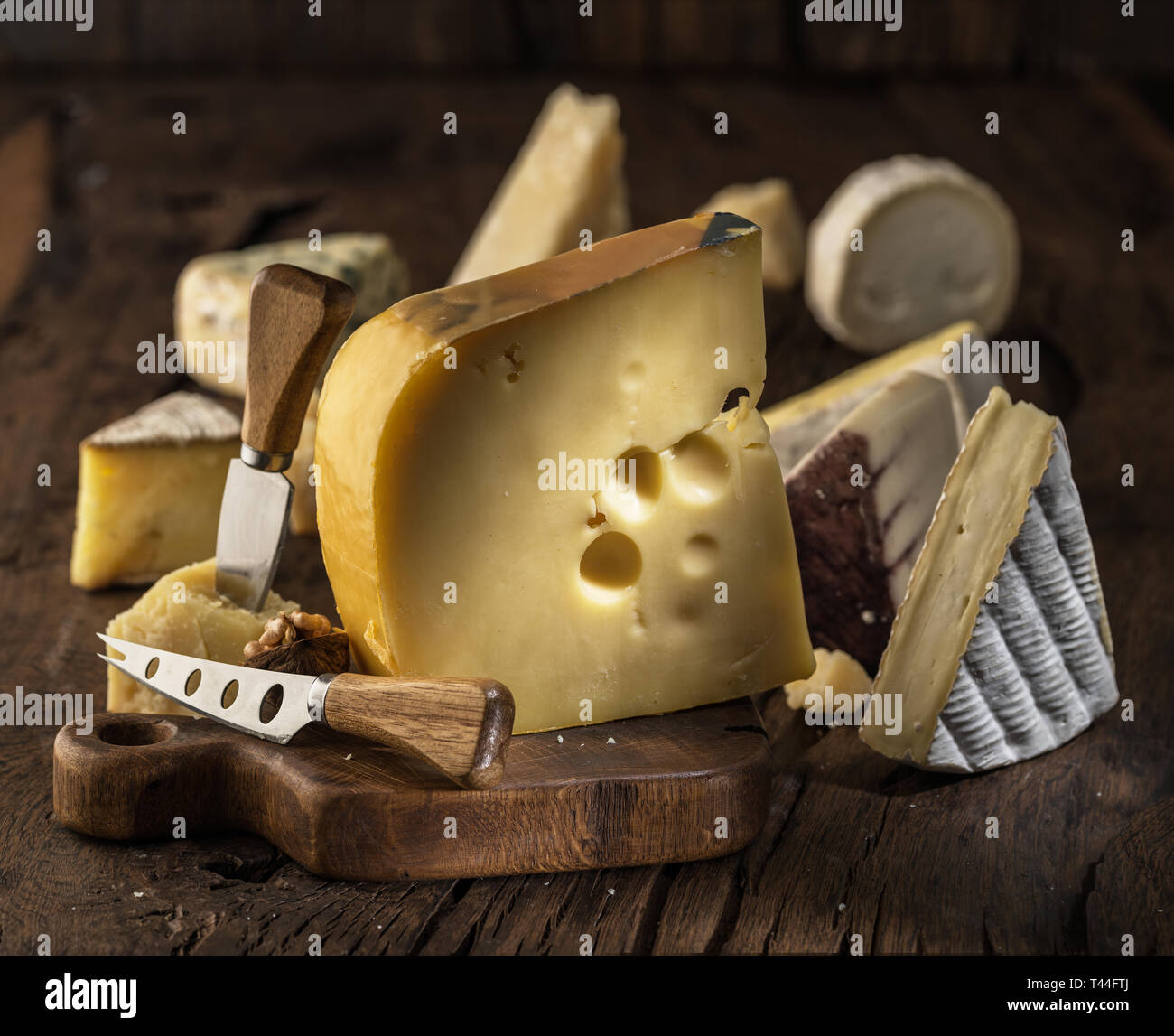Piece of cow's milk Maasdam cheese on wooden board. Range of cheeses at ...