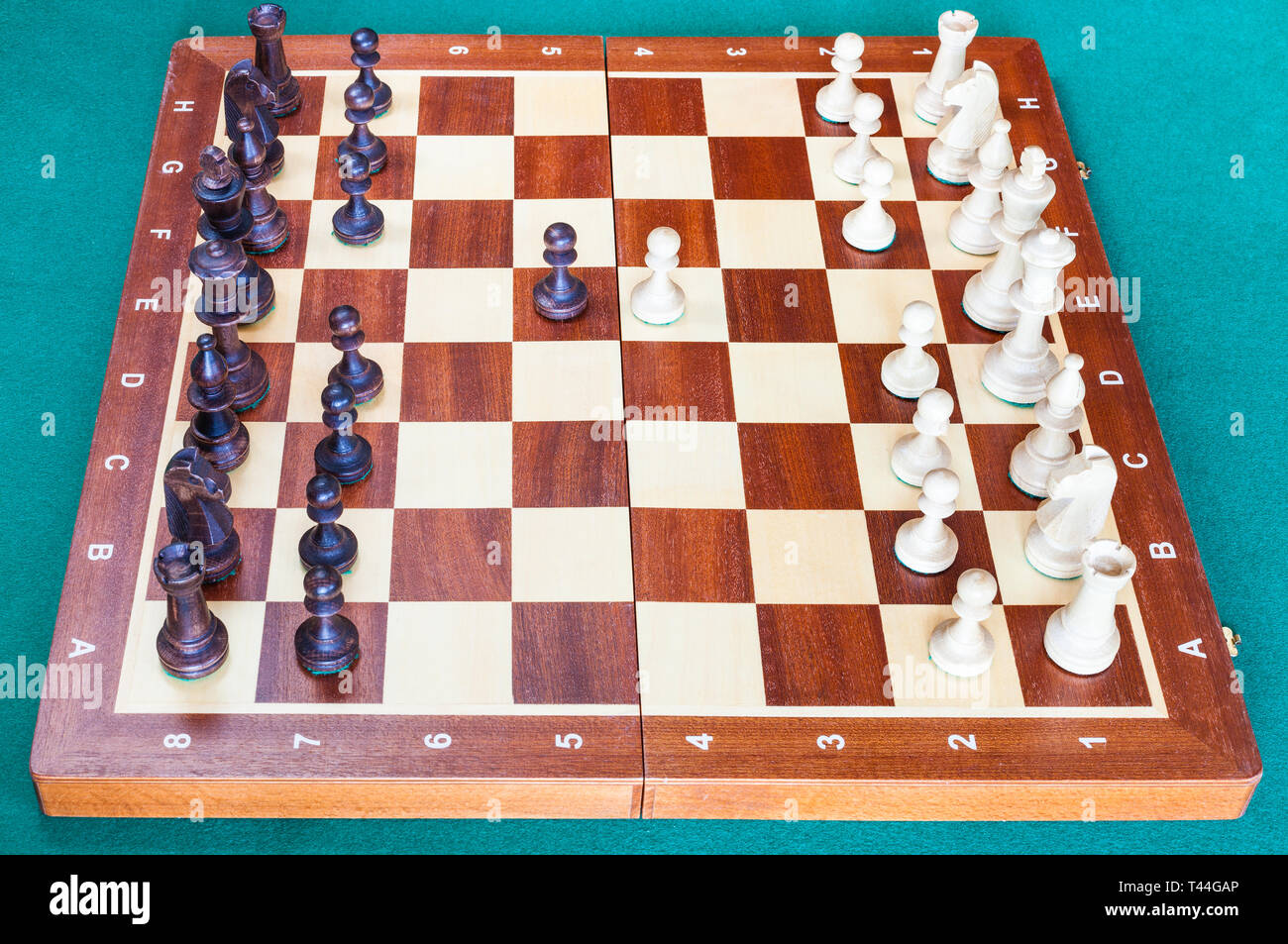 side view of wooden chessboard with first chess pawn moves on green ...