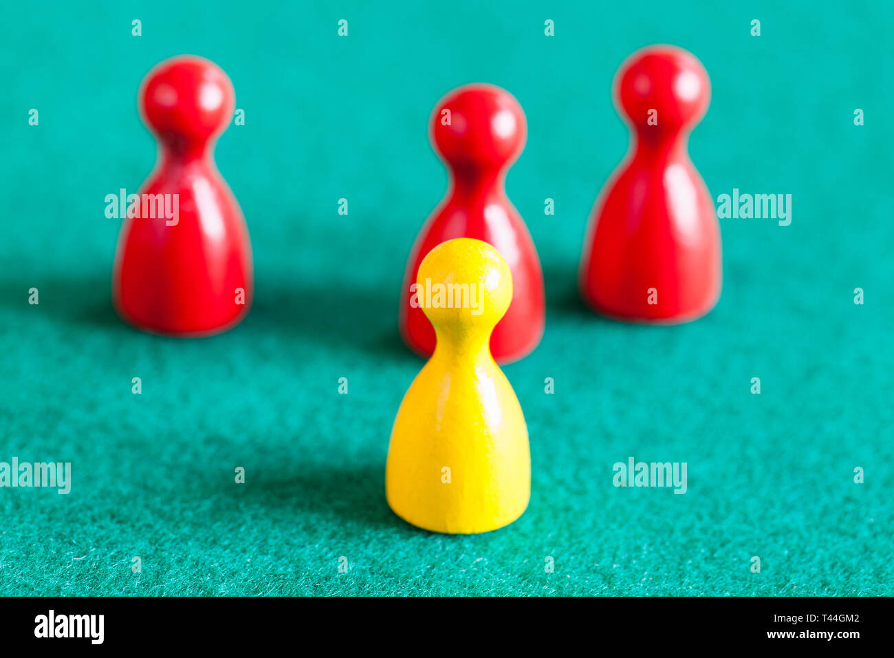 concept scene - one yellow pawn in front of three red pawns on green ...