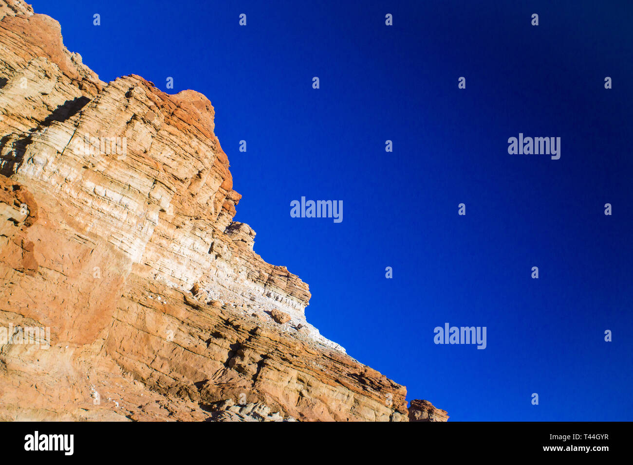 Red and orange rocks form a cliff face above the hot sands of the ...