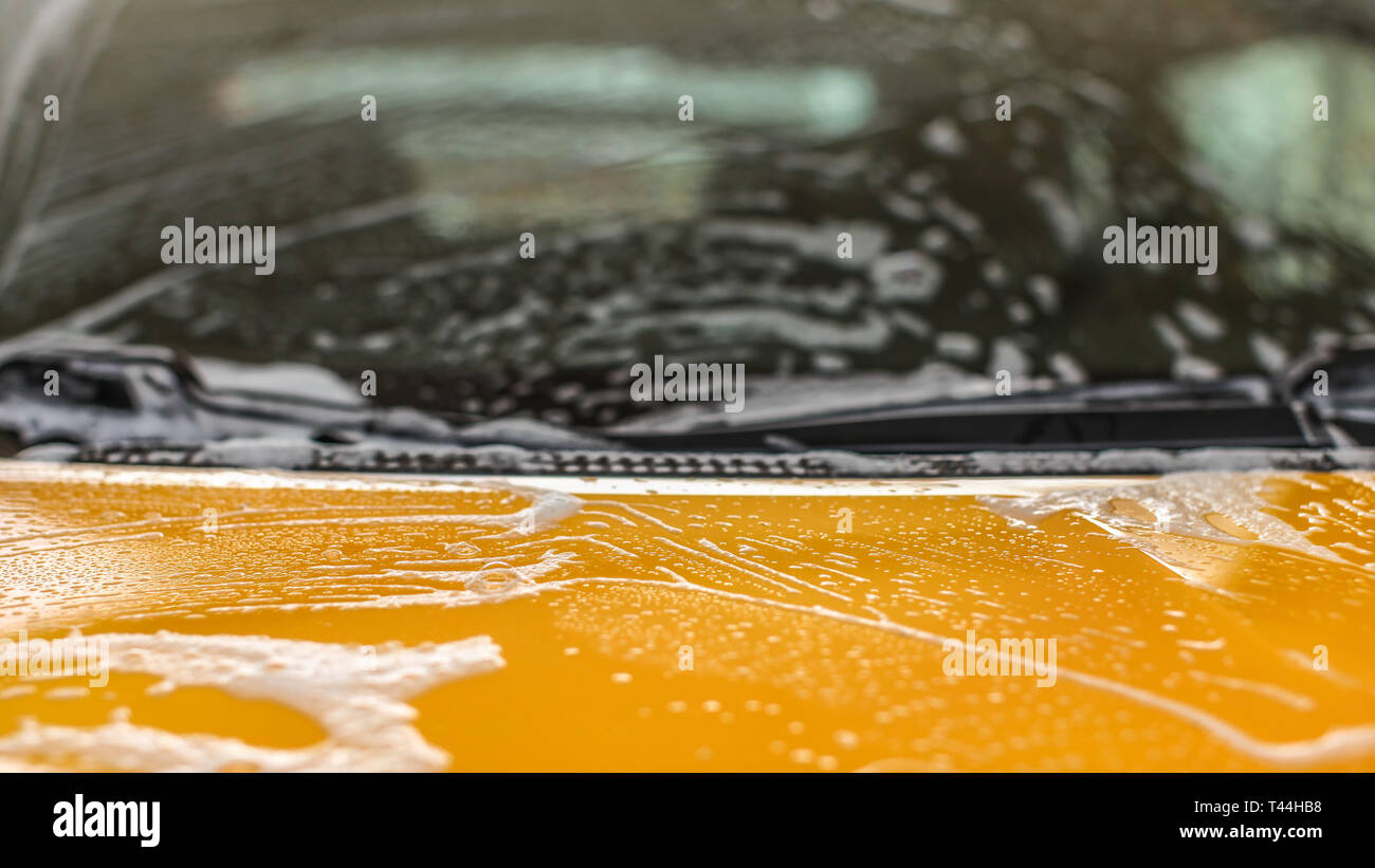 Closeup detail - front hood of yellow car covered with white shampoo ...