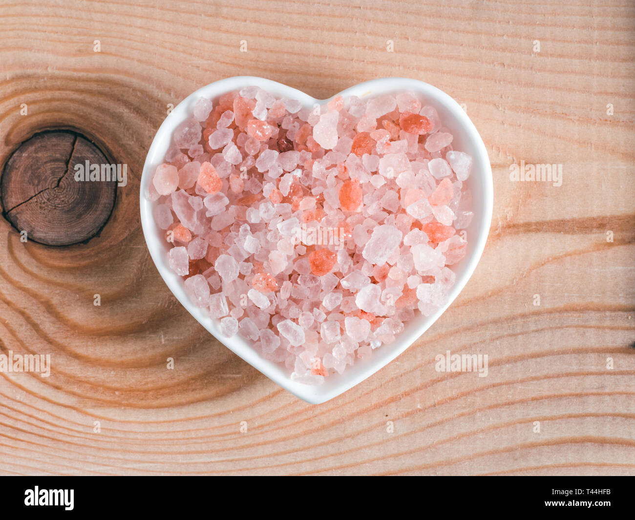 Himalayan pink salt in hearth-shape bowl on wooden background. Copy ...