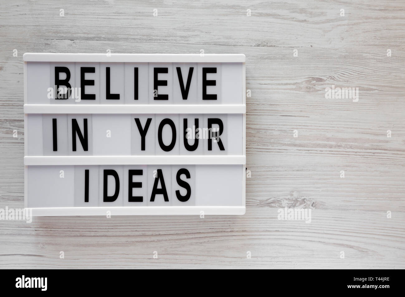 Top view, 'Believe in your ideas' words on lightbox over white wooden ...